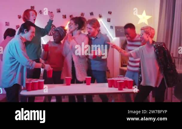 Young man and woman playing beer pong at home party with multiethnic ...