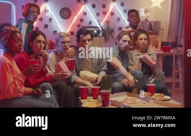 Group of young diverse friends sitting together on couch, eating ...