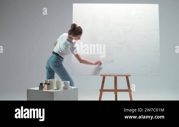 Female artist applies a layer of white primer on a large canvas in a ...