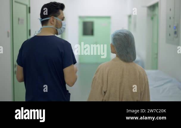 Back view of doctor and patient walking to operating room in clinic ...