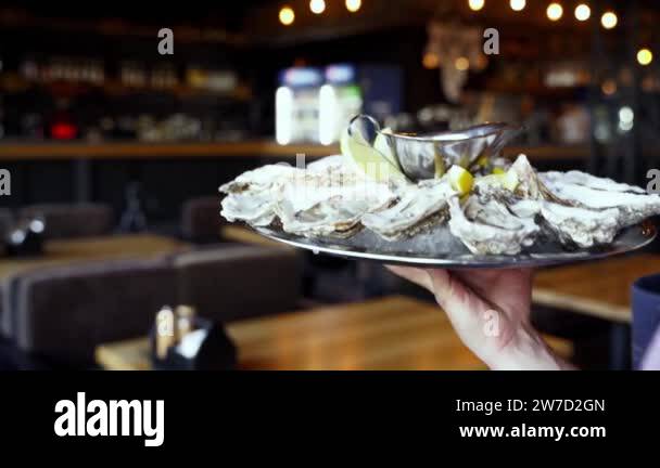 Waiter carries a tray of served oysters on ice with lemon for luxury ...