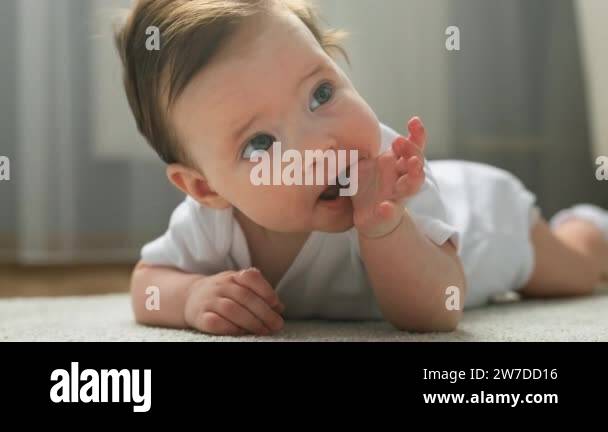 Cute newborn baby girl lies on her stomach and bites her fingers with ...