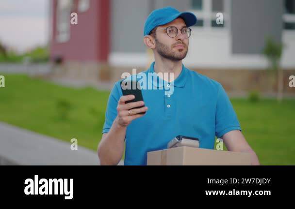 The postman with glasses carries the parcel and looks at the delivery ...