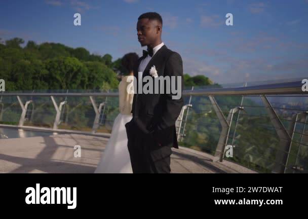 Frustrated African American groom in elegant suit on summer bridge with ...