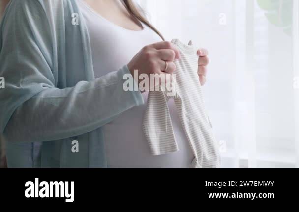 4k Pregnant mother holding baby clothes in hands. Happy Expectant ...