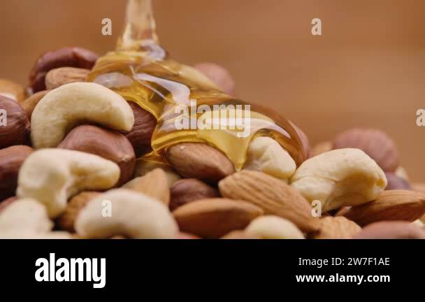 Trickle of golden honey flows down a pile of nuts in slow motion. Honey ...