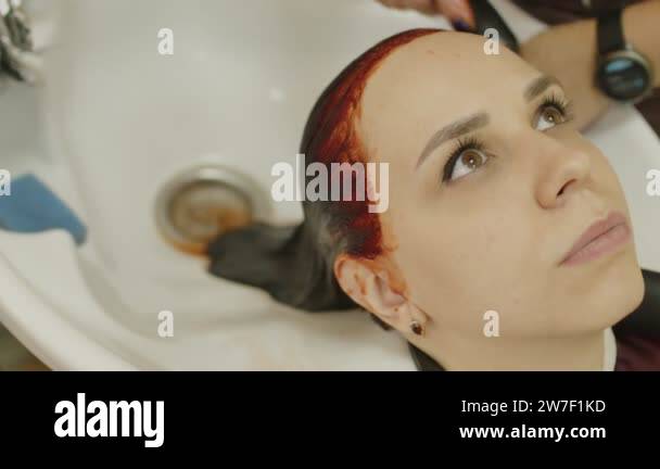Young woman sits, putting head over sink during hair care procedure in ...