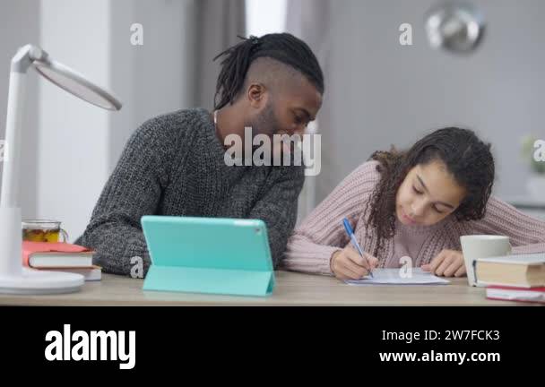 African American father making facepalm gesture as teen daughter making mistake doing homework ...