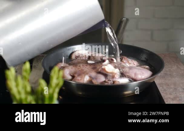 Pouring water into hot frying pan with boiling octopus. Boil liquid ...