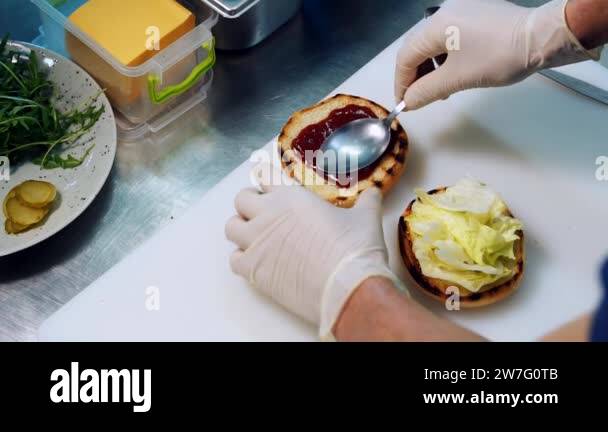 Chef spreads the red sauce with a spoon on a bun. Cook smears sauce on ...