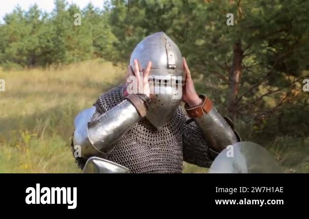 A medieval warrior in full armor, takes off his helmet. A medieval ...