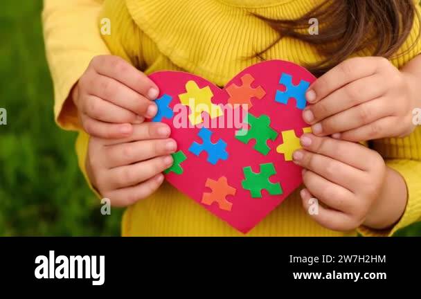 Two girls are holding a red heart with colorful puzzles inside, made ...