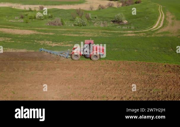 Red tractor with harrows is loosening the ground to protect soil from ...