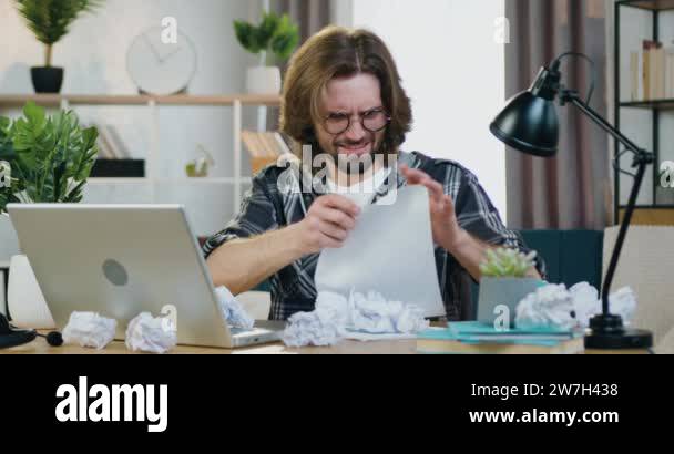 Frustrated angry young bearded office worker in glasses sitting at his ...