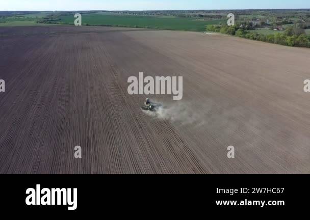Aerial view of tractor with harrow system plowing ground on cultivated ...