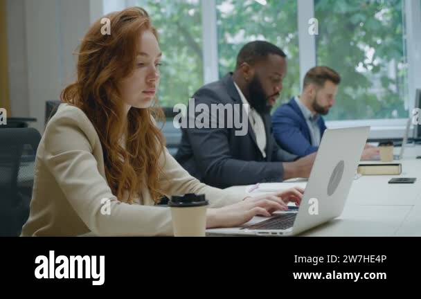 Young businesswoman in formal wear working on a laptop in busy office ...