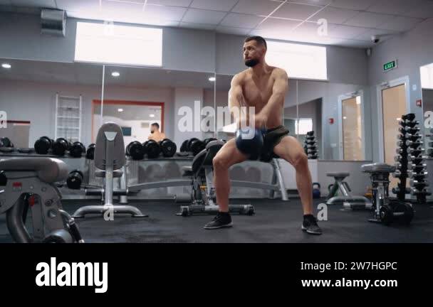 The muscular man performs semi-positions with a dumbbell in his hands ...