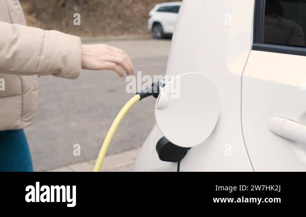 Woman coming to the electric vehicle and unplugging power supply cable ...