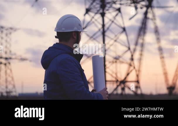 An electrician on the background of high towers of power plants looks ...