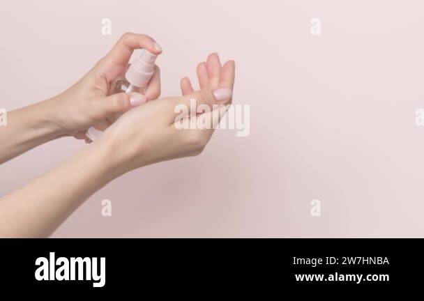 Female hands using hand sanitizer spray dispenser over light pink ...