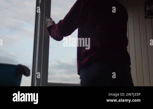 Washing window glass at home. A young long-haired man with a beard is ...