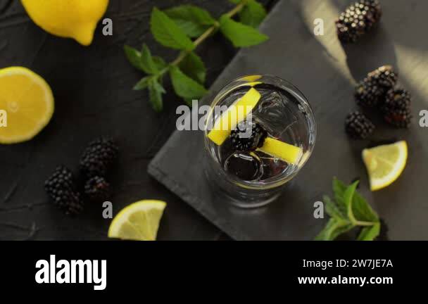Summer bramble and mint cocktail in a glass on black stone table. Hand ...