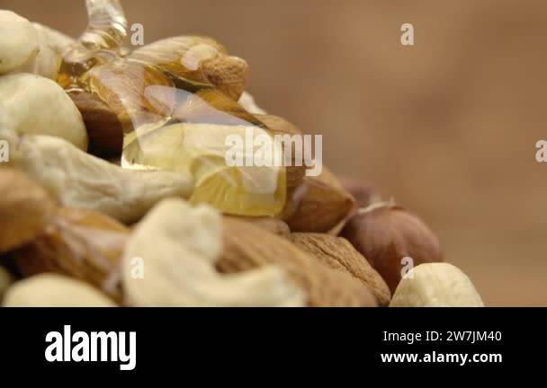 Trickle of golden honey flows down a pile of nuts in slow motion. Honey ...