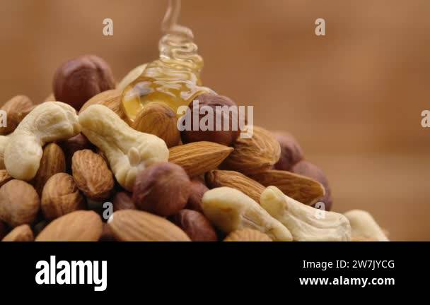 Trickle of golden honey flows down a pile of nuts in slow motion. Honey ...