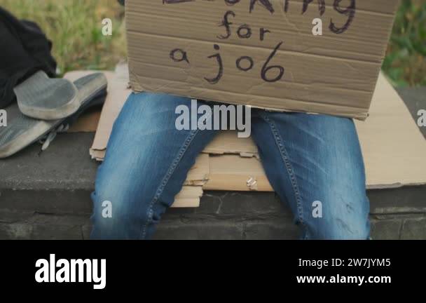 Homeless man with belongings on the street sits on parapet, looking for ...