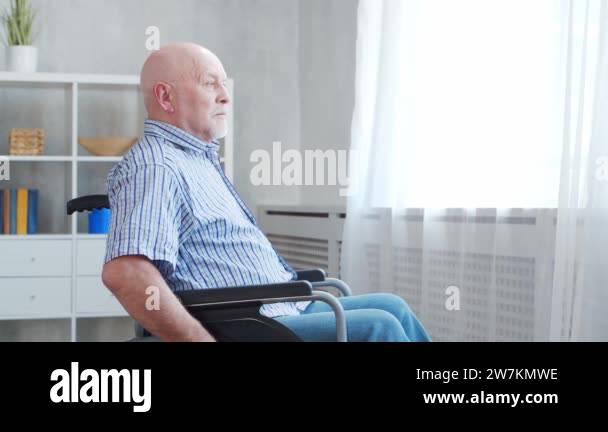Disabled old man is sitting in a wheelchair at home alone. A ...