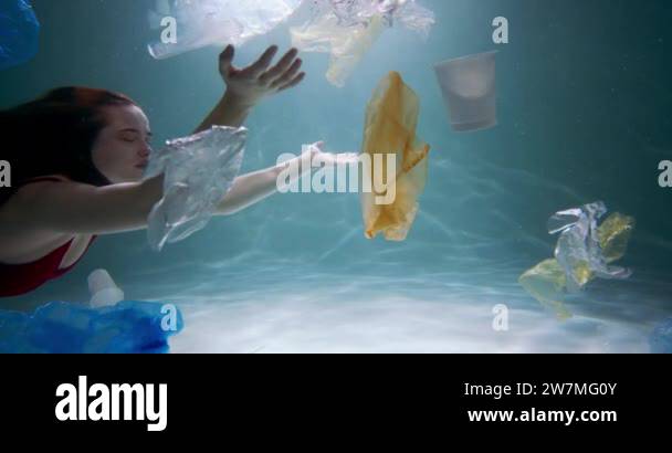 Beautiful female tourist swims under water through single use packaging ...