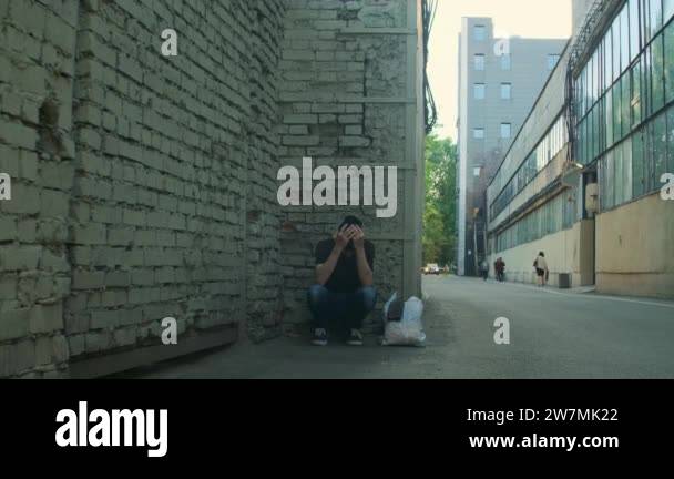 Homeless man on the street leaned on the wall covering his face by ...