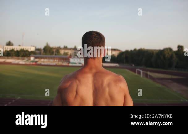 A young muscular man jumping in place on the stadium and flexes his ...