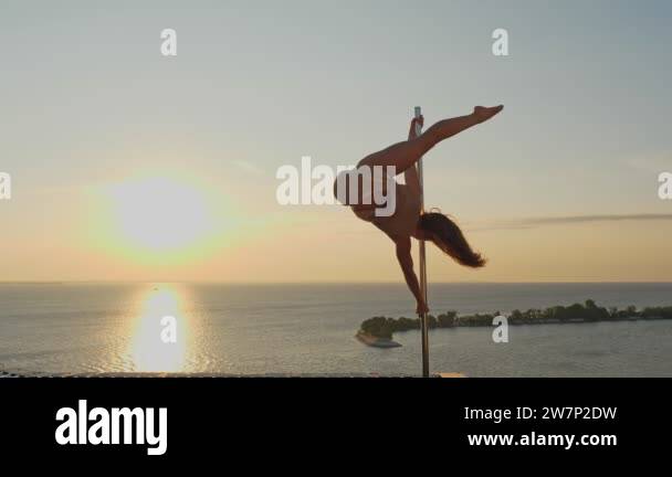 pole dance. silhouette. fit female gymnast, in beige leotard, performs ...