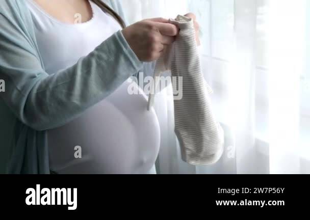 4k Pregnant mother holding baby clothes in hands. Happy Expectant ...