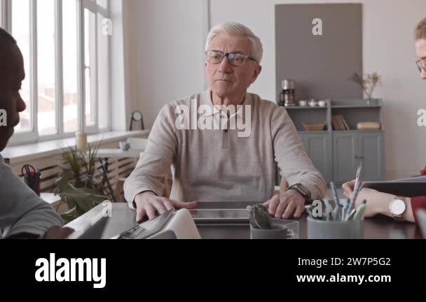 Zooming out of older Caucasian CEO sitting at head of table in office ...