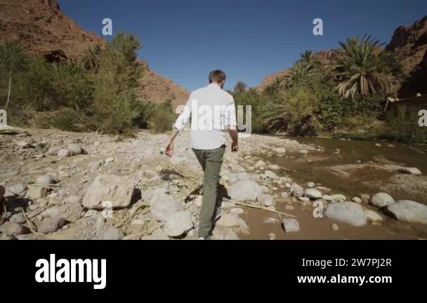 Tracking footage of man going in rough terrain along river. Jumping ...