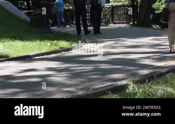 Unrecognizable people walking in a shadow of city park in sunny summer ...