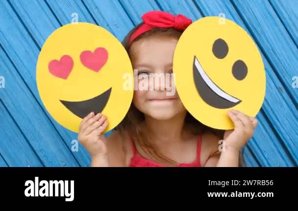 A little girl covers her face with a cardboard smiley face with happy ...