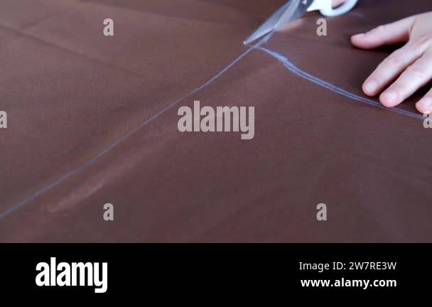 Woman hands with scissors cutting brown fabric according to markings on ...