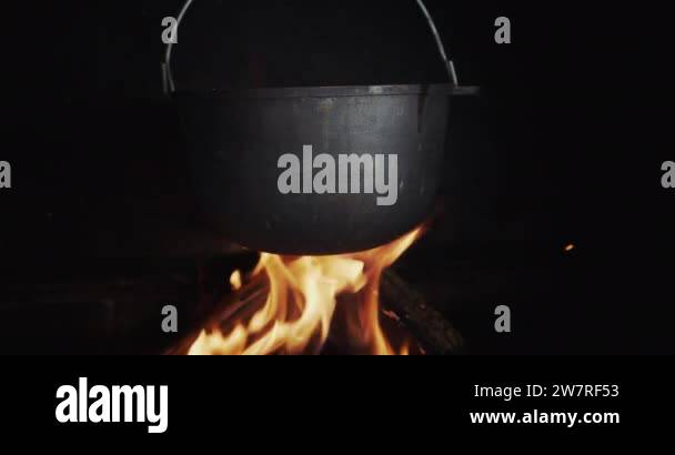 A cast-iron vat of boiling broth hangs in a wood-burning stove over an ...