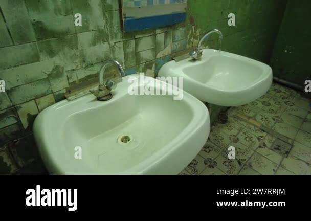 Water drips from the tap into the sink into a room with crumbling tiles ...