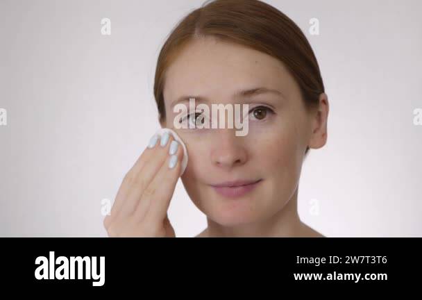 Beautiful woman strokes face skin with cotton pad. Young woman applies ...