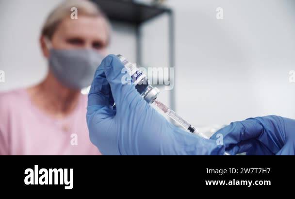 Close-up on doctor hand in blue glove using syringe and vaccine flask ...