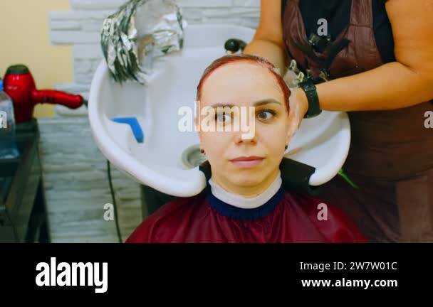 Young woman sits, putting head over sink during hair care procedure in ...