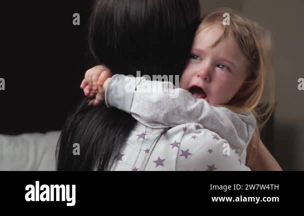 Mom soothes her daughter, child cries in room in arms of his mother. Loving young mother hugs ...