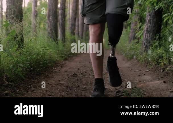 Disabled man with a prosthetic limb walks in the forest. Close-up of ...