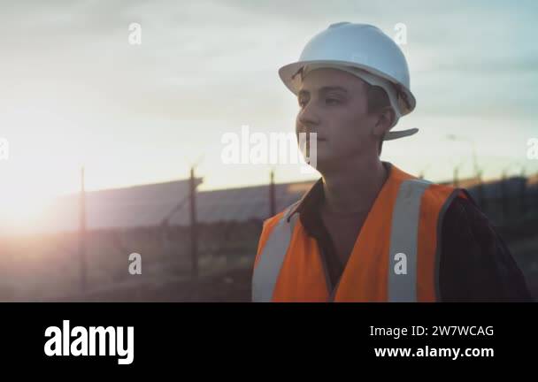 Portrait of a young engineer next to solar panels during sunset. Checks ...