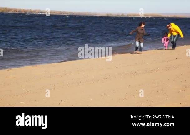 family of mum, daddies and daughter runs one after another on sandy to ...