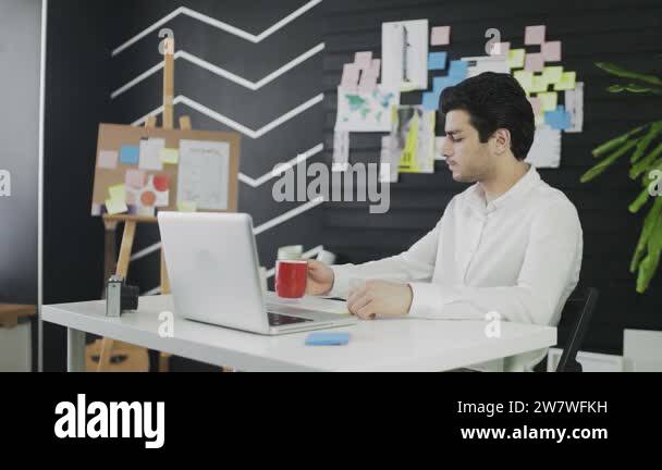 A young man of Caucasian appearance is sitting at a computer looking ...